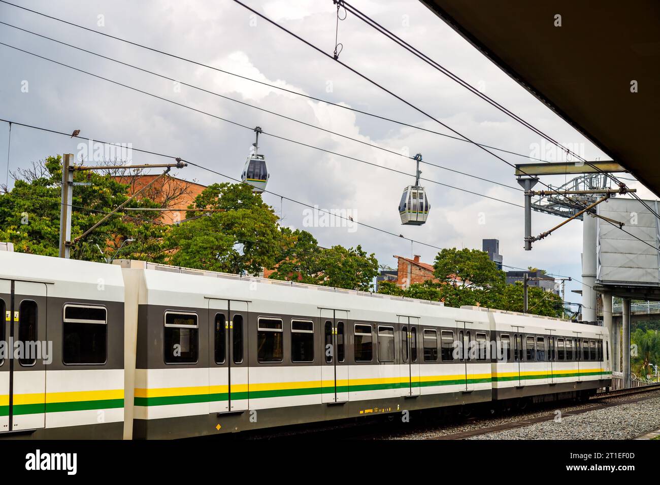 Medellin metro leaving a station with metrocables in the background ...
