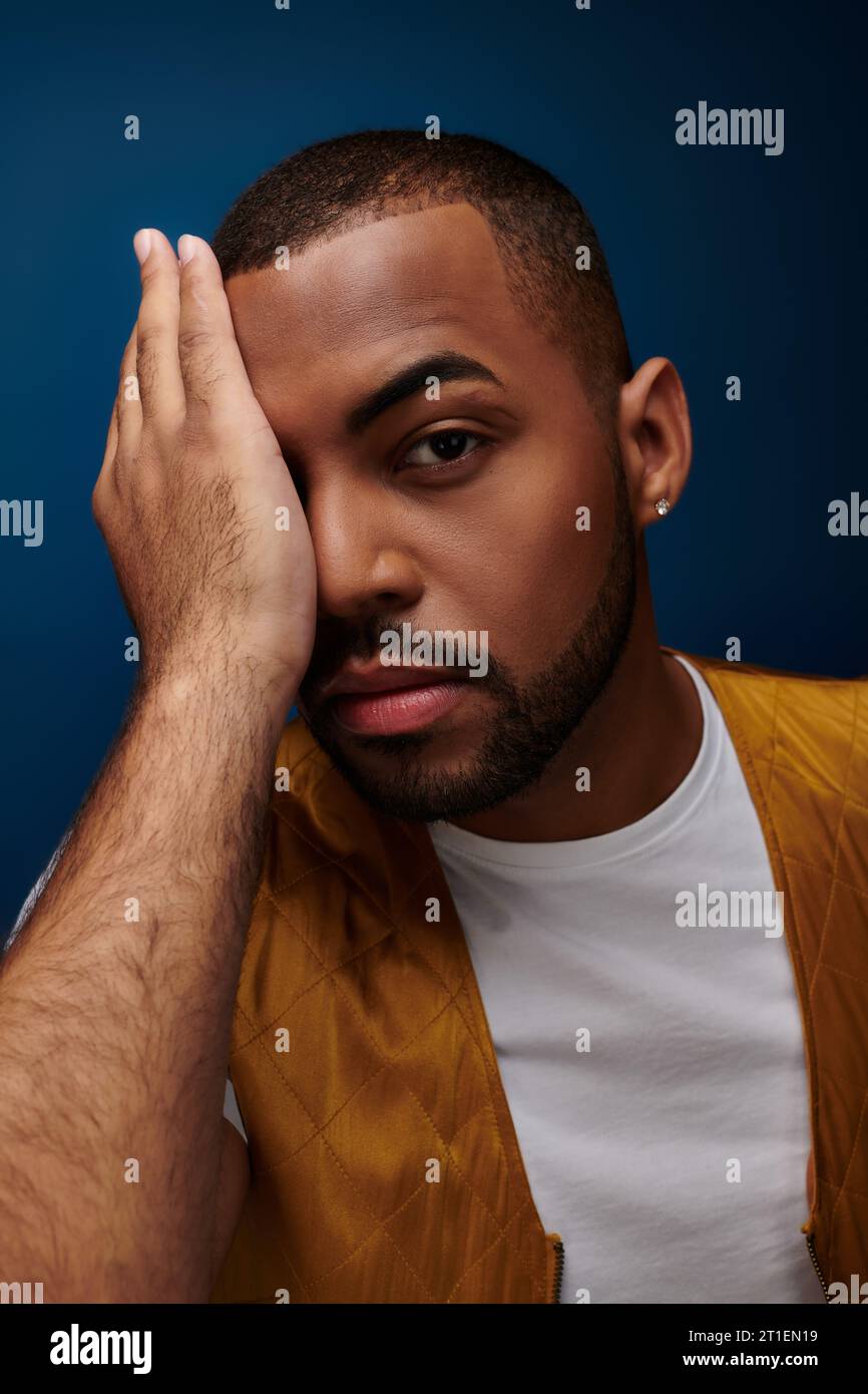 portrait of young man on dark blue backdrop with his palm on face ...