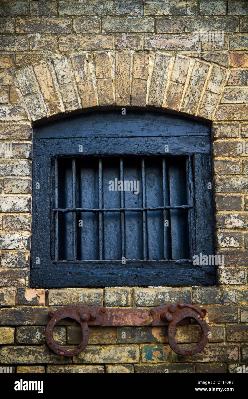 An ancient brick prison wall with a boarded up window with metal bars ...