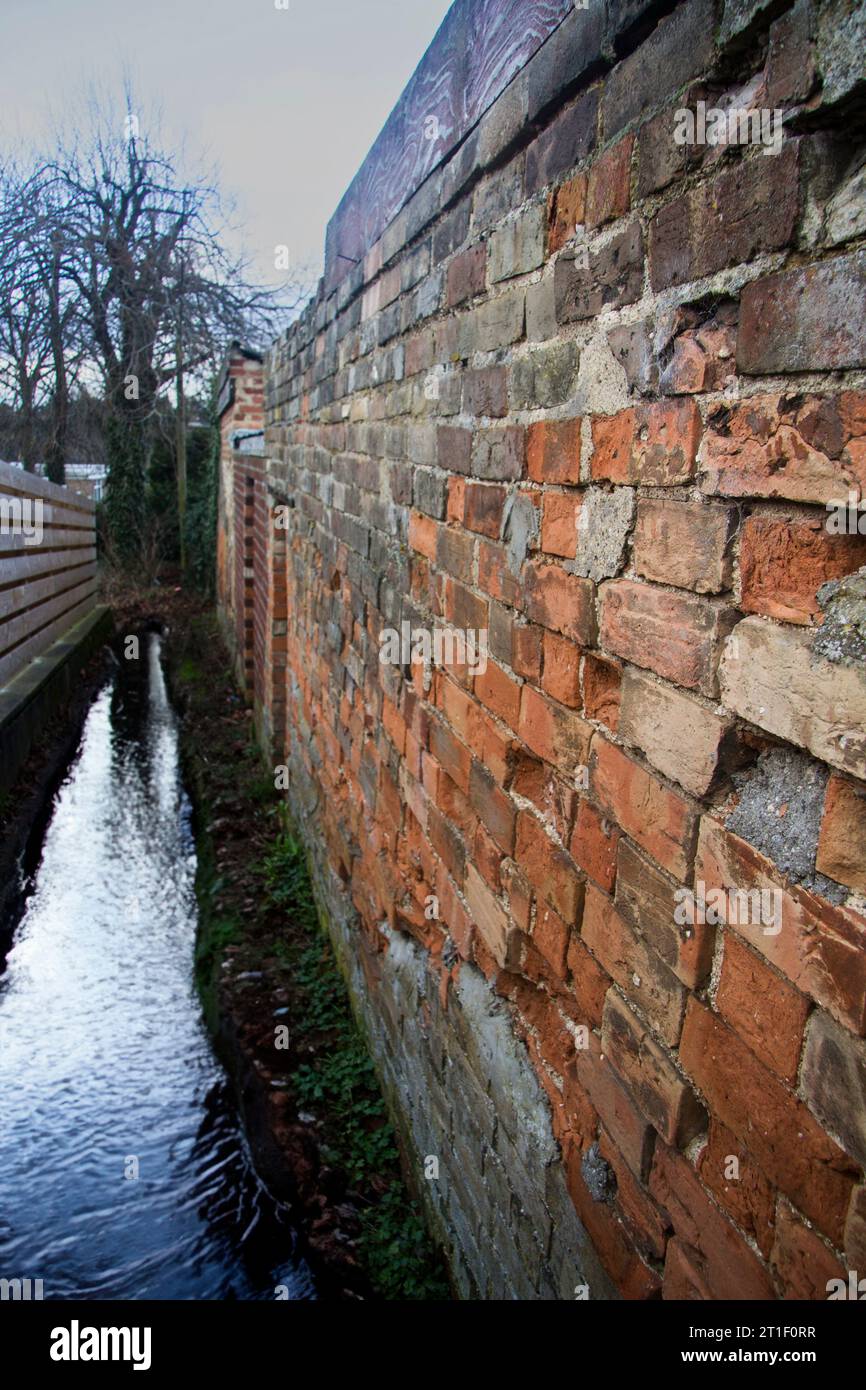 A flooded ancient footpath with an old worn brick wall to the side ...