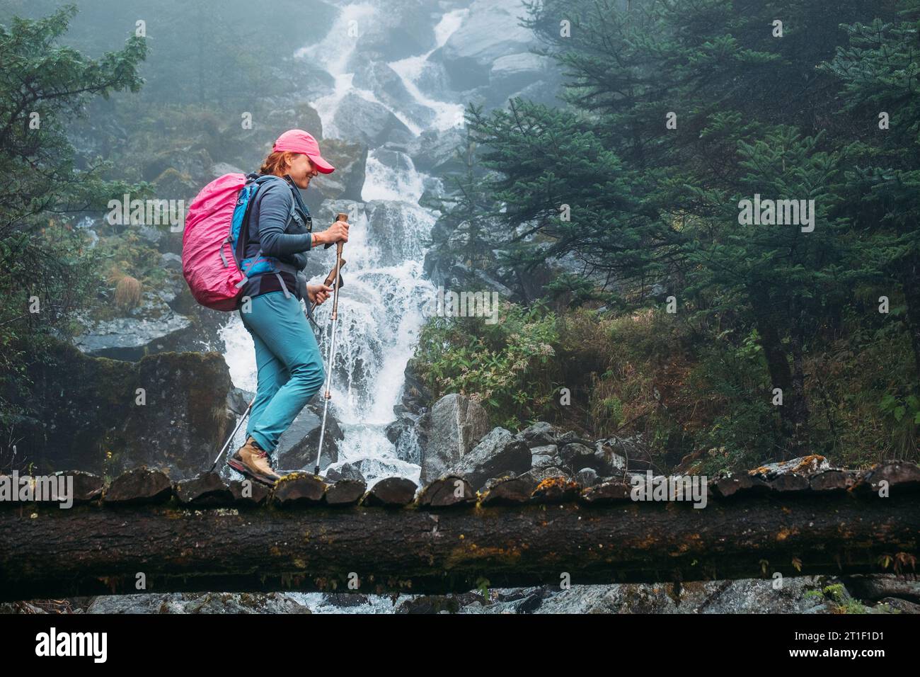 Young woman with backpack and trekking poles crossing wooden bridge ...