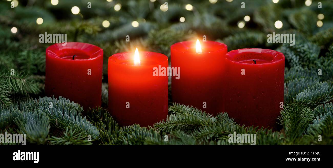 Red Advent candles, two burning, with fir branches and bokeh lights ...