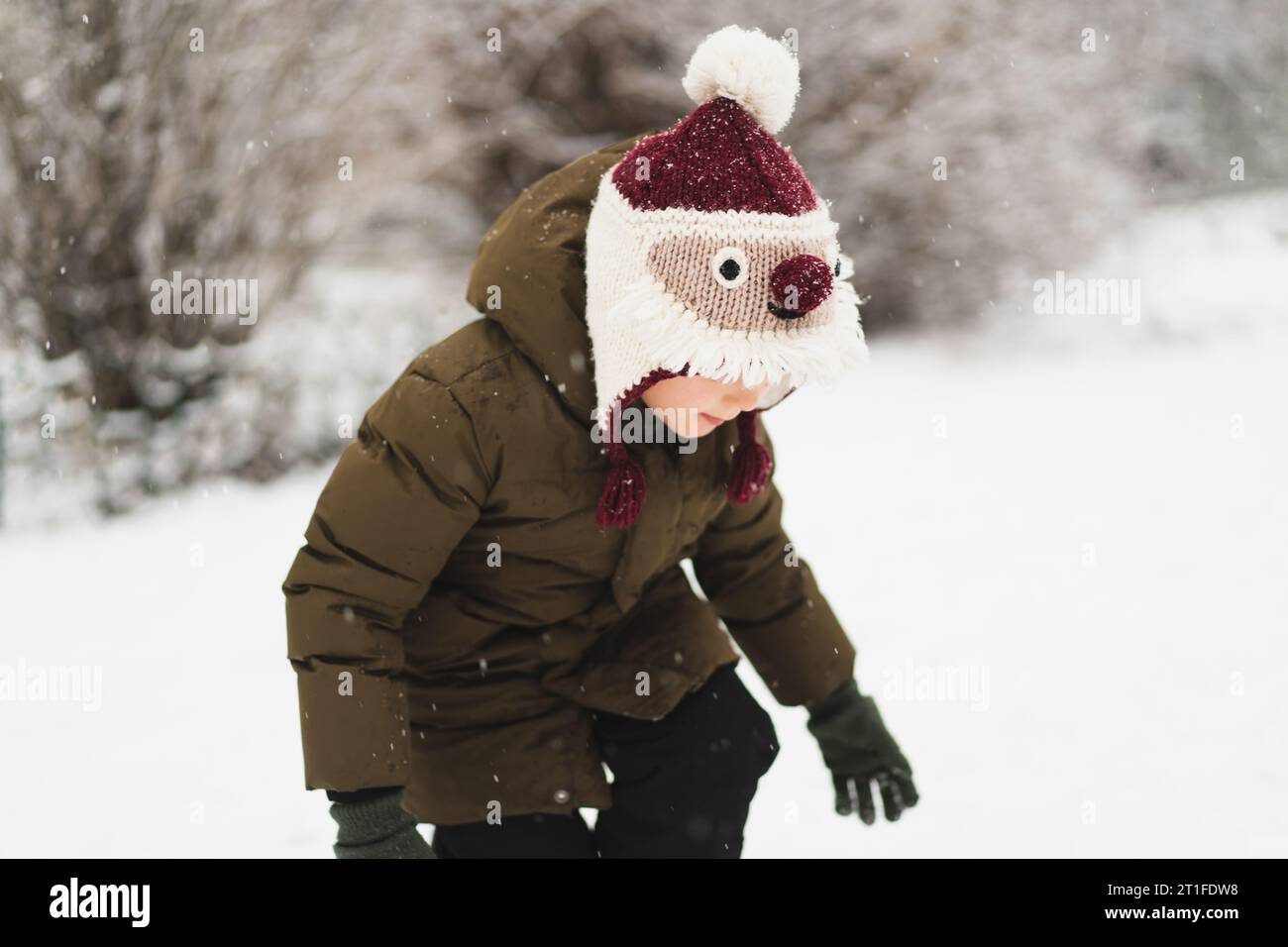 Cute little boy in funny winter hat walks during a snowfall. Outdoors ...