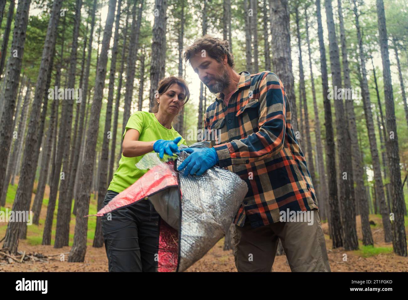 Two dedicated individuals work together in a pine forest, picking up discarded waste. Their ...