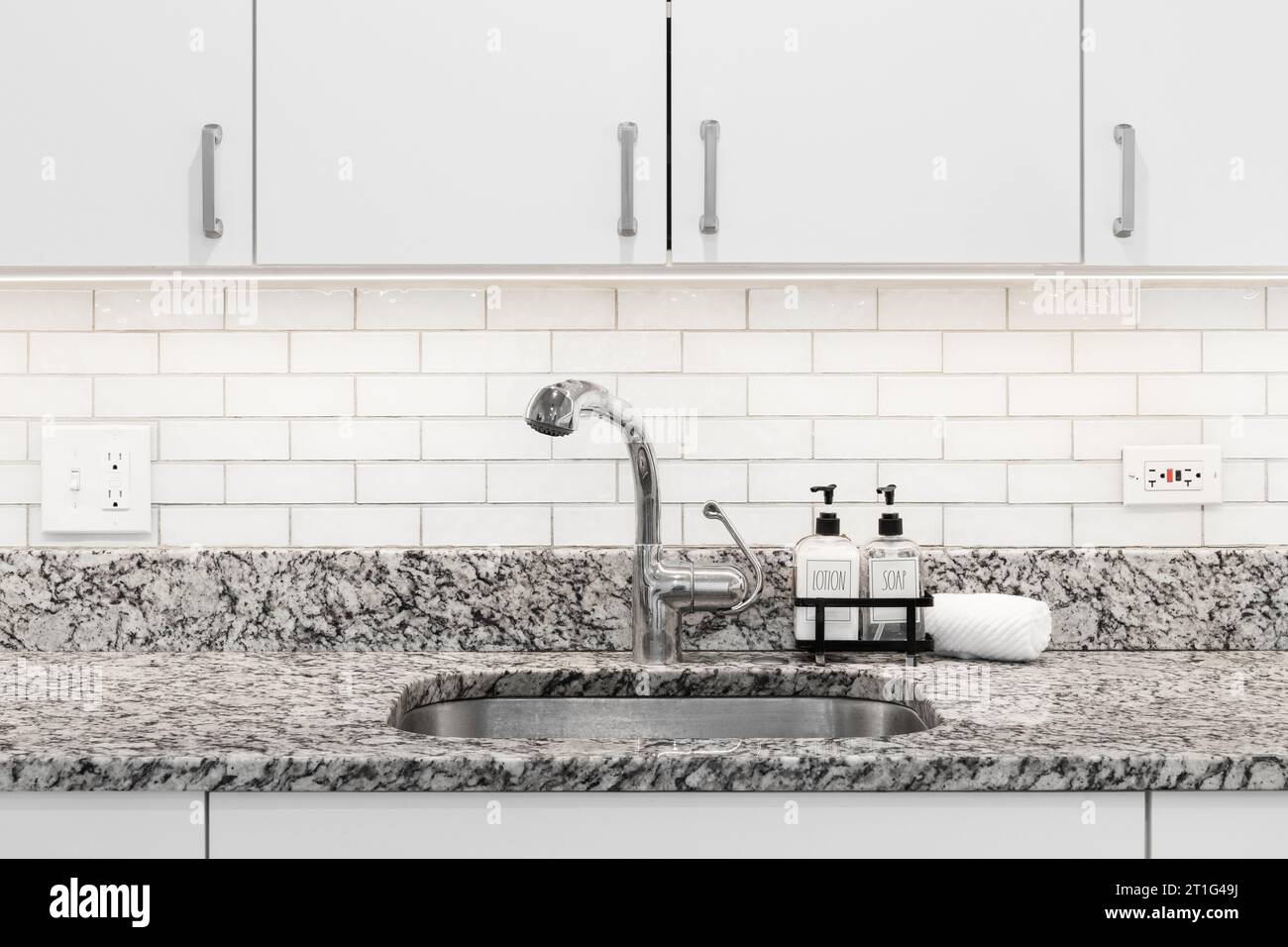 A kitchen sink detail with a chrome faucet, marble countertop, white ...