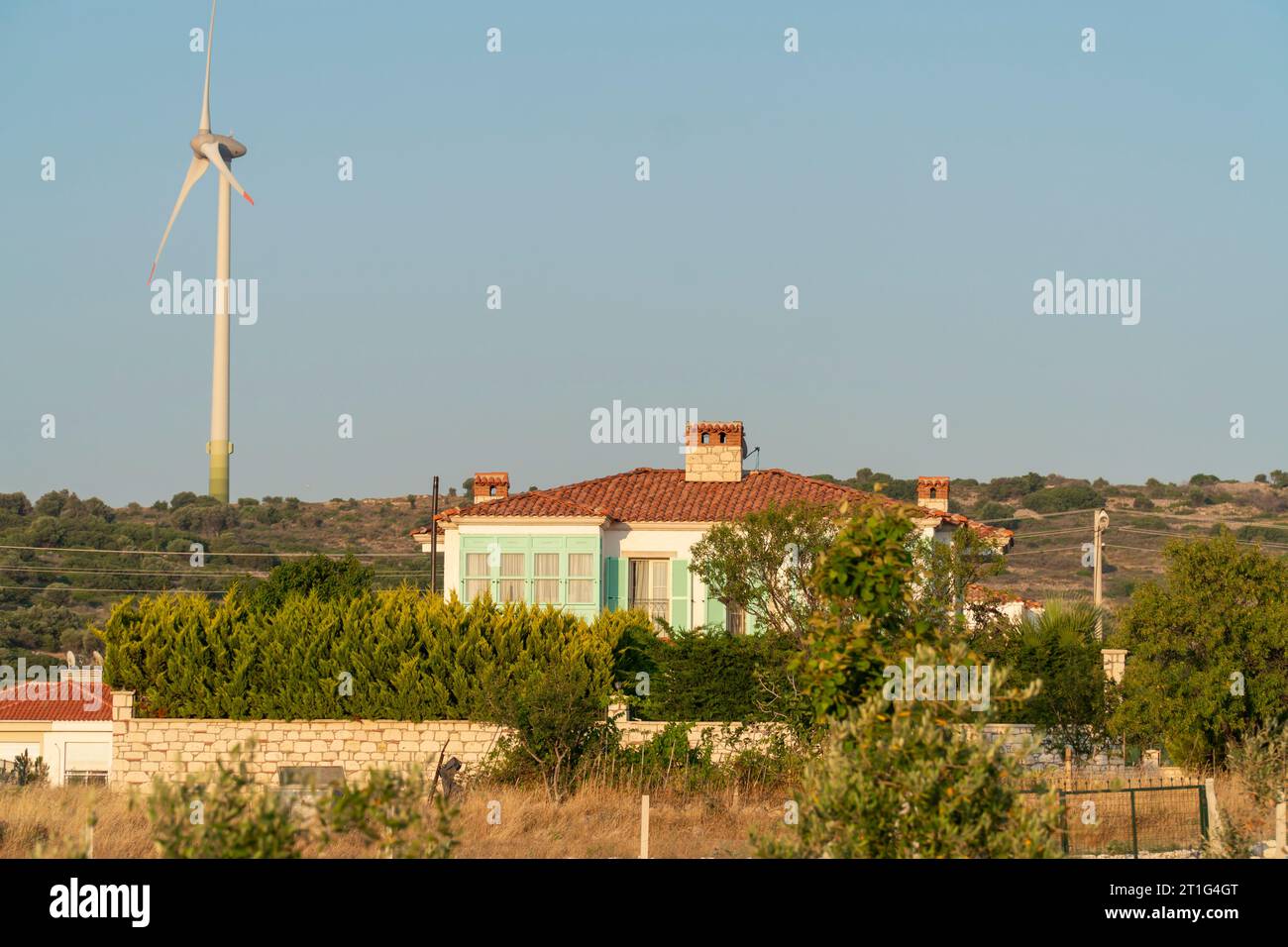 House with a wind turbine in the behind, evening spring landscape ...