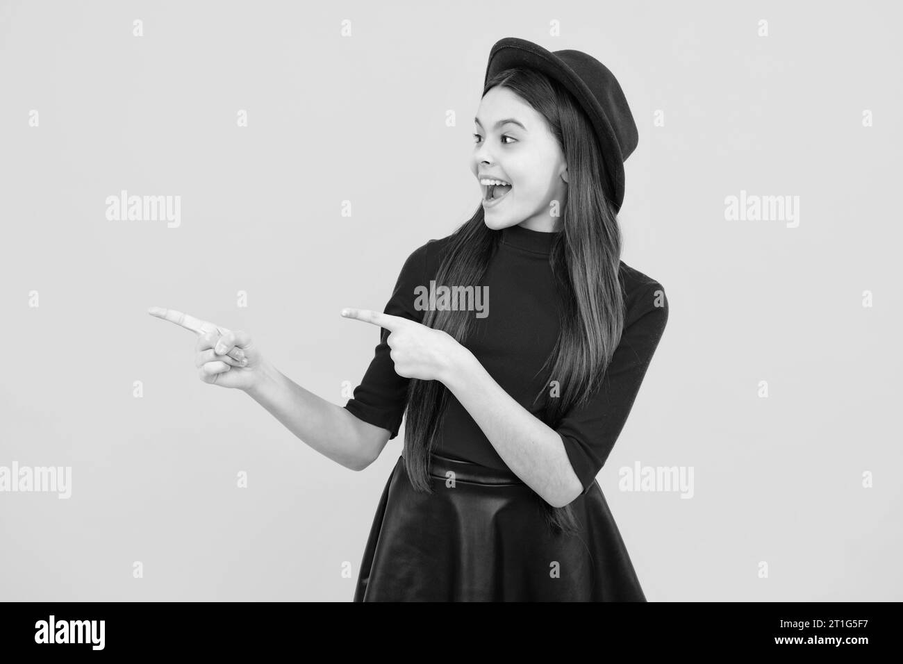 Positive teenager child points aside with cheerful expression, shows ...