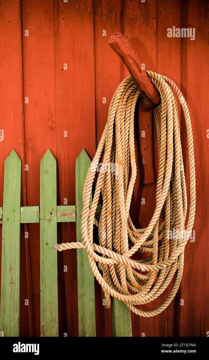 Coiled rope hanging on the wooden hook at the wooden red wall Stock ...