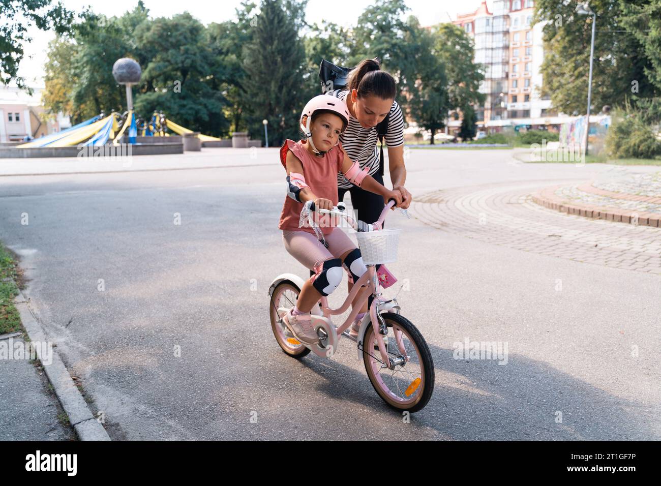 Mother learning child girl to ride a bike in the park in the summer ...