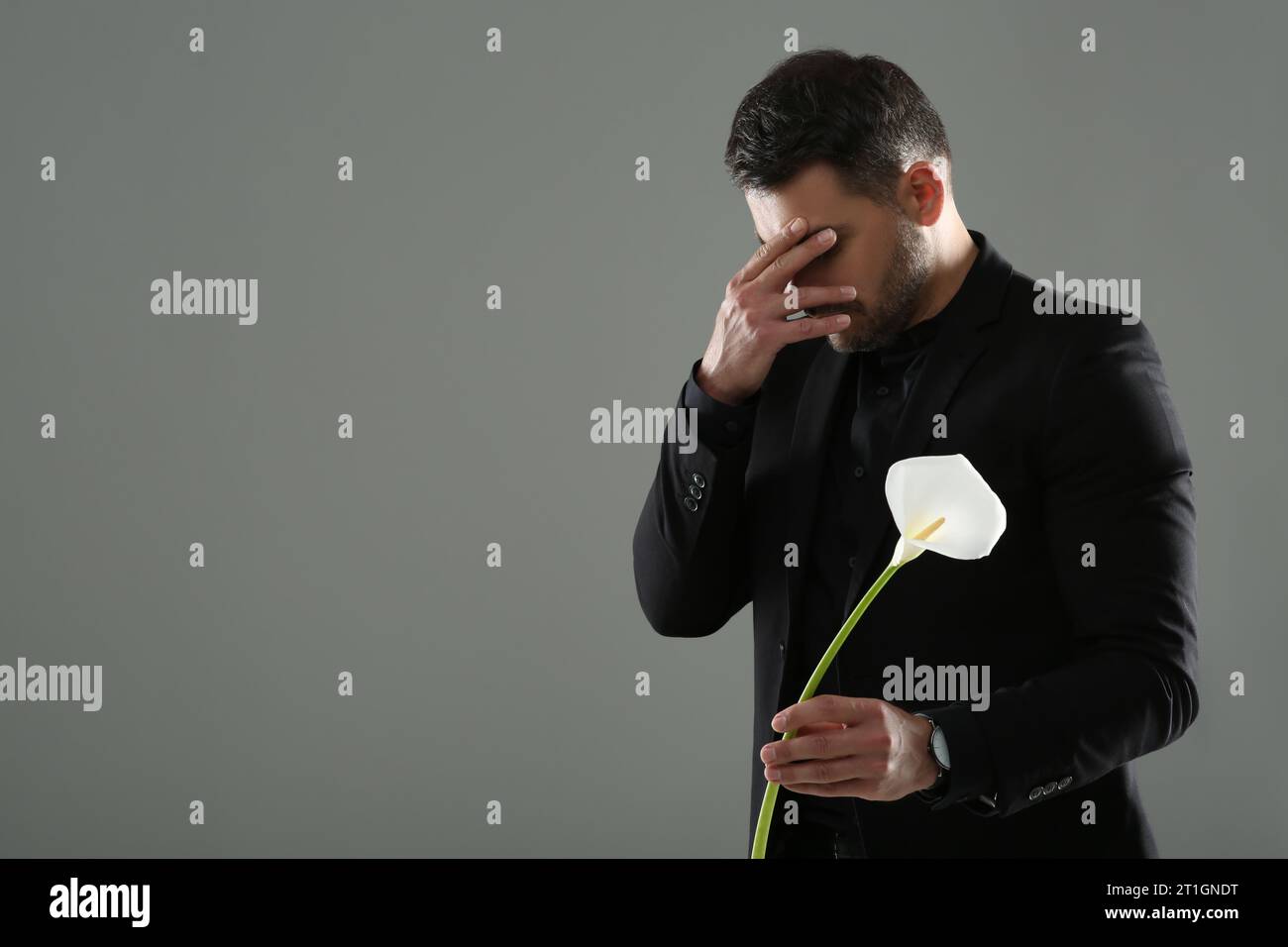 Sad man with calla lily flower mourning on grey background, space for ...