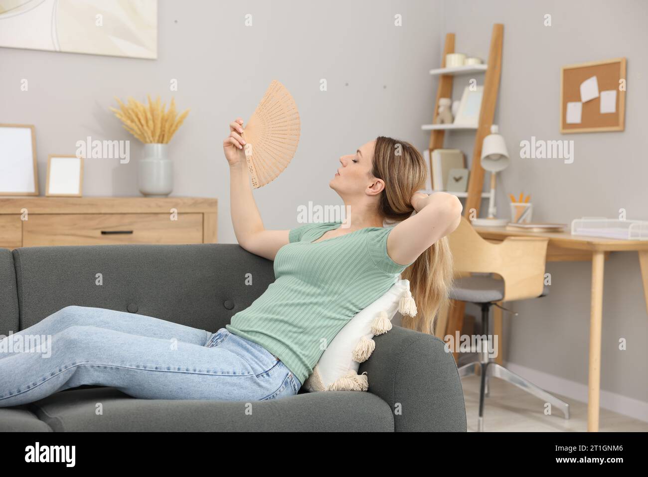 Woman waving hand fan to cool herself on sofa at home Stock Photo - Alamy