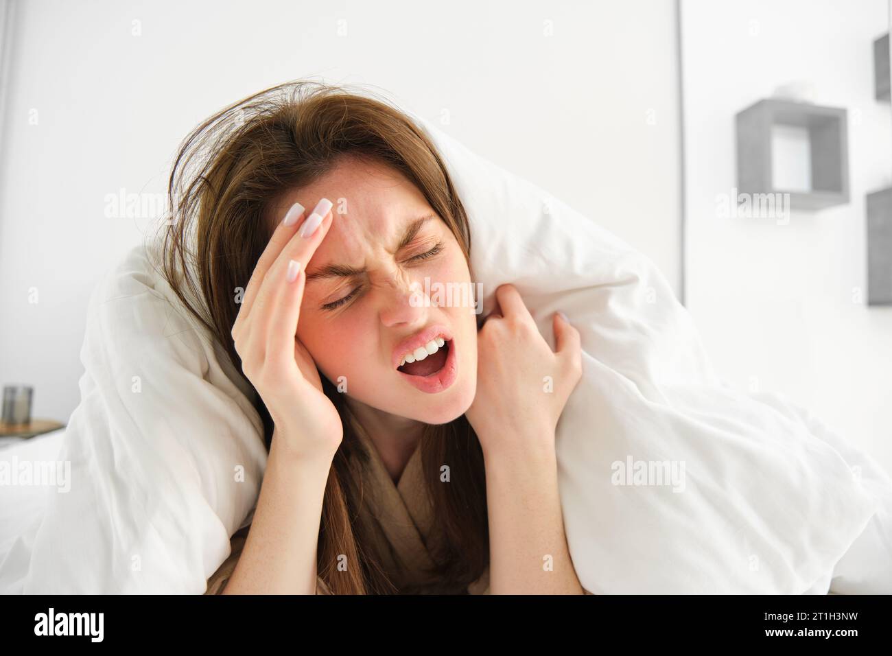 Woman suffering headache in morning, lying in bed under blankets ...