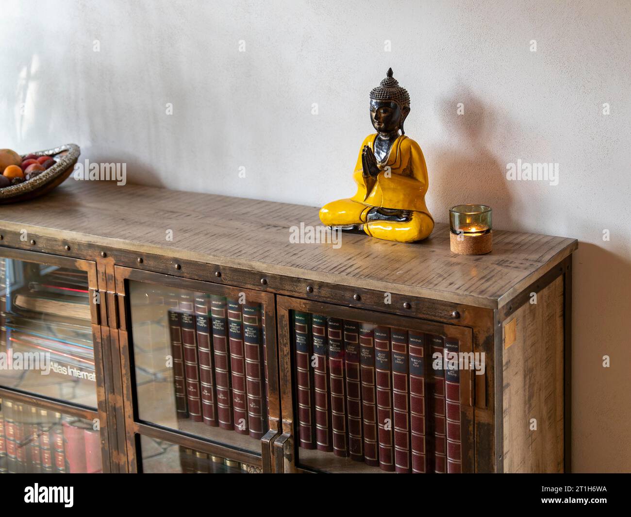 Books and encyclopaedias in old glass case with metal, Buddha figure on ...