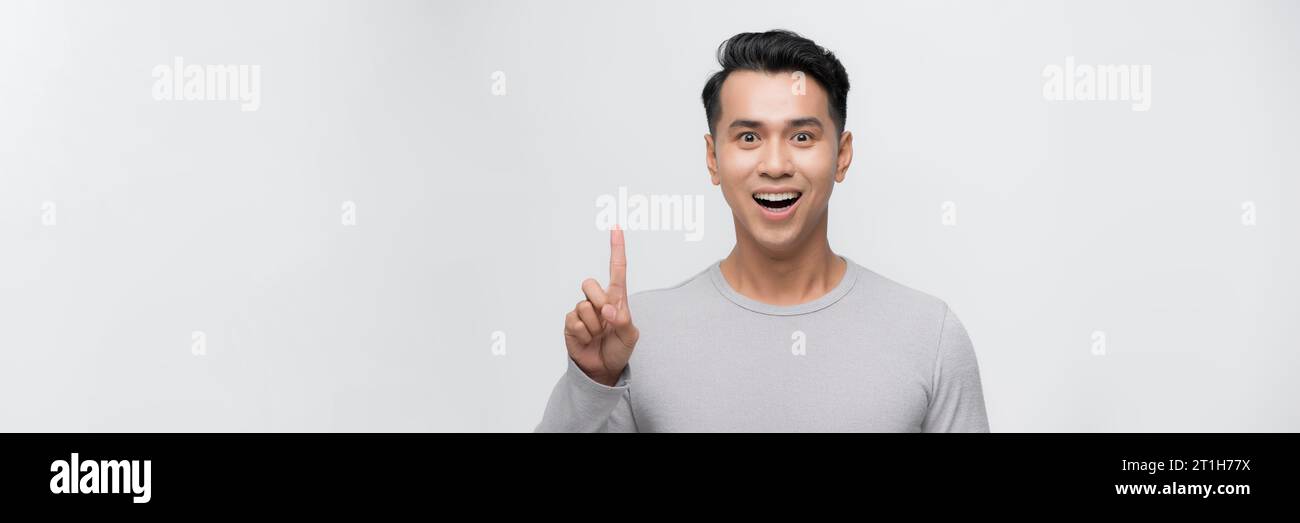 Attractive young man pointing up with his finger isolated on gray ...