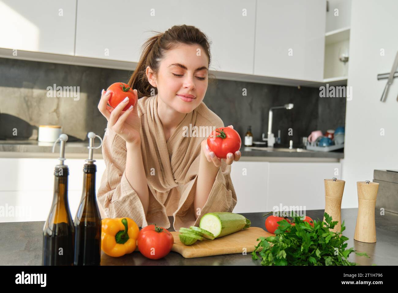 Portrait of woman cooking at home in the kitchen, holding tomatoes ...