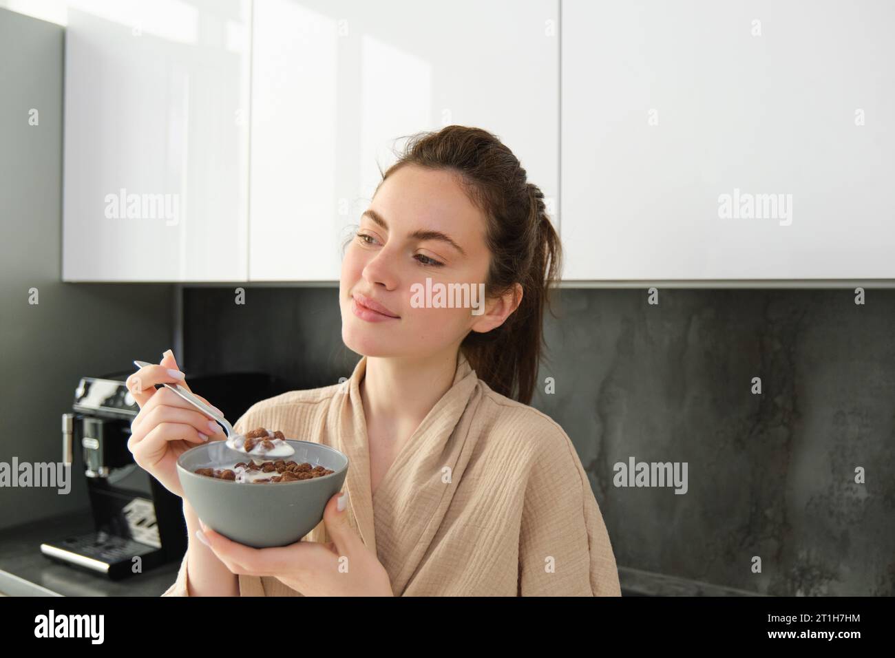Happy mornings. Gorgeous young woman eating cereals with milk, standing ...