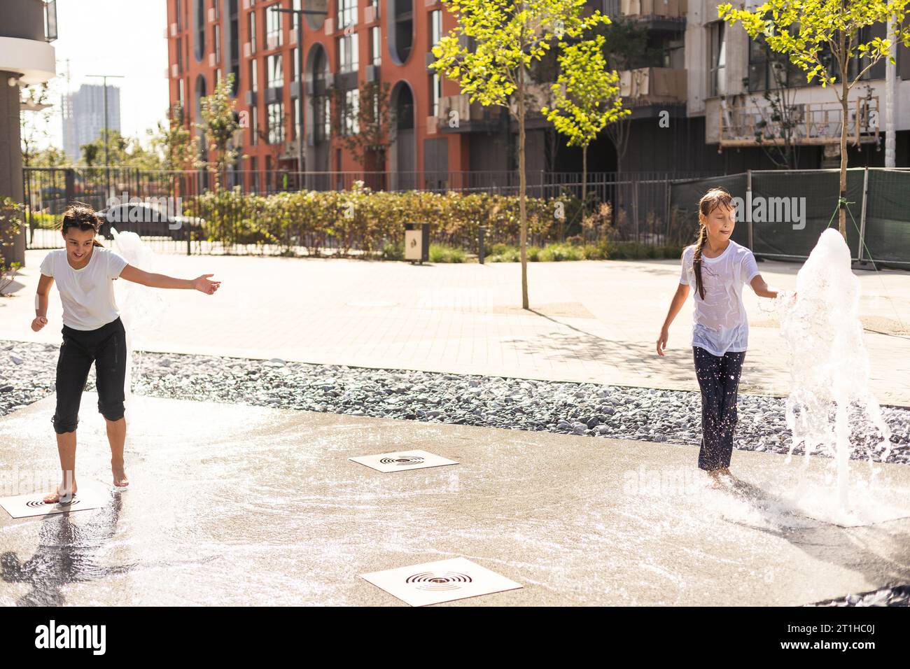 Cheerful young teen girl in city fountain, girl in wet clothes is ...