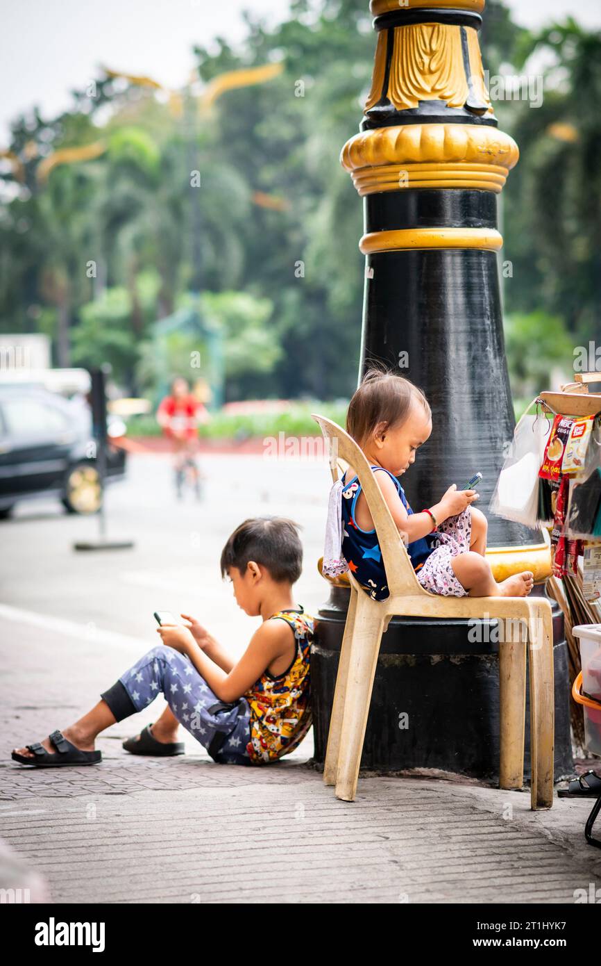 Two young Filipino children enjoy something on their mobile phones sat ...