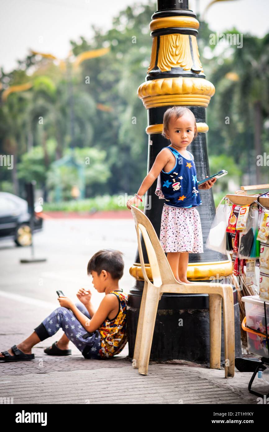 Two young Filipino children enjoy something on their mobile phones sat ...