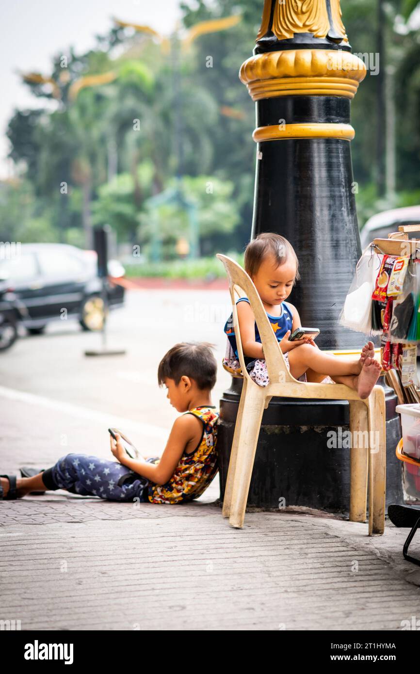 Two young Filipino children enjoy something on their mobile phones sat ...