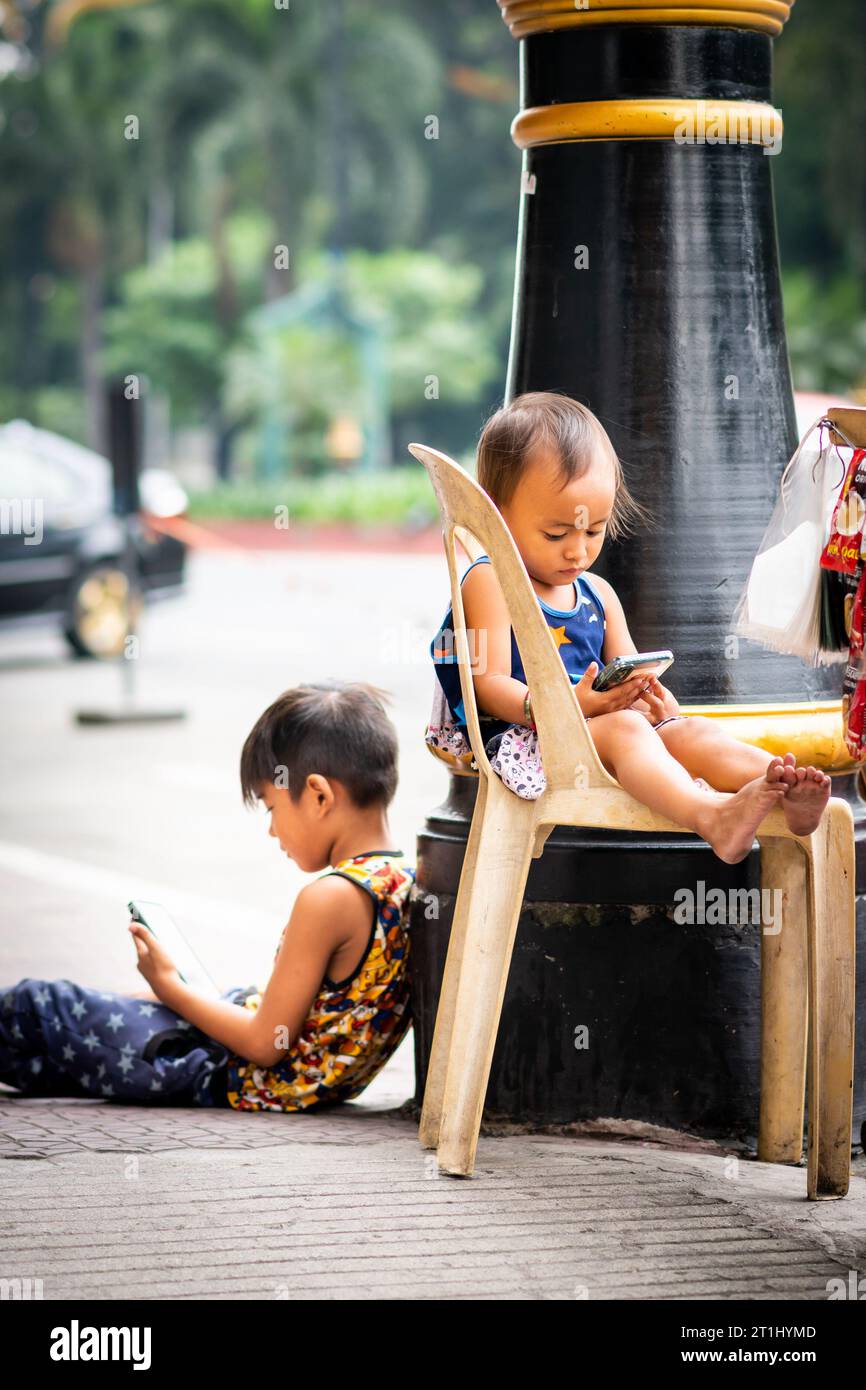 Two young Filipino children enjoy something on their mobile phones sat ...