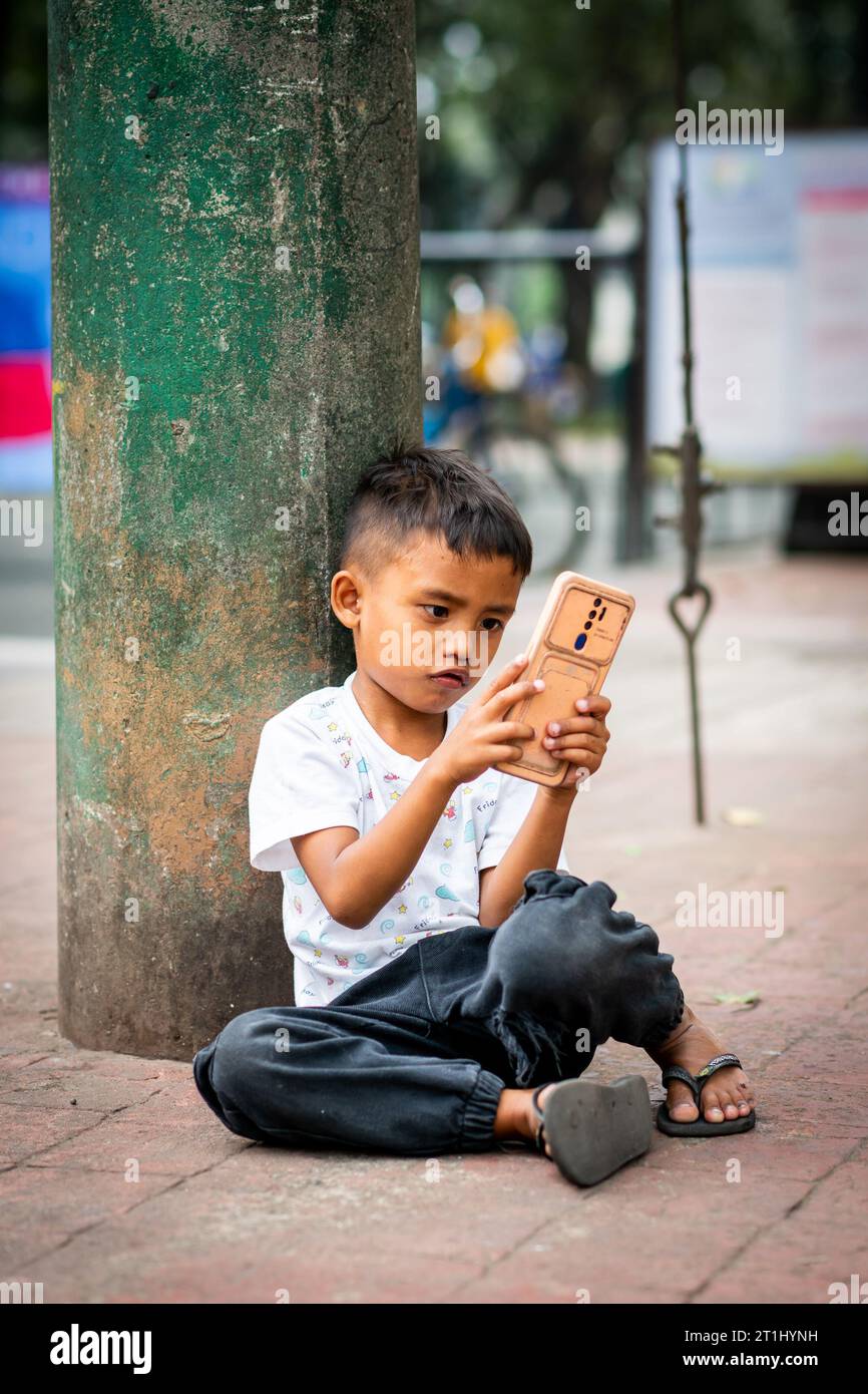 A young Filipino boy enjoys something on his mobile phone sat outside ...
