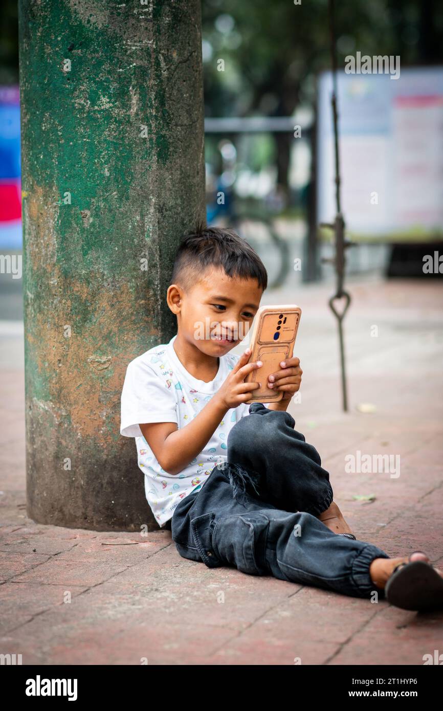 A young Filipino boy enjoys something on his mobile phone sat outside ...