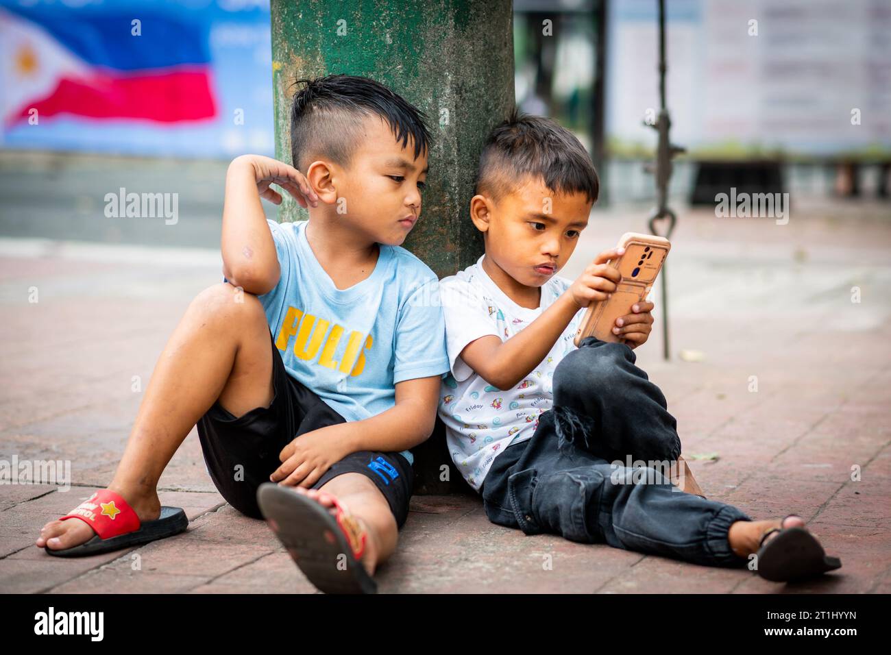 Two young Filipino boys enjoy something on their mobile phone sat ...