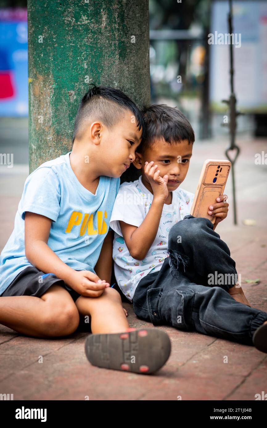Two young Filipino boys enjoy something on their mobile phone sat ...