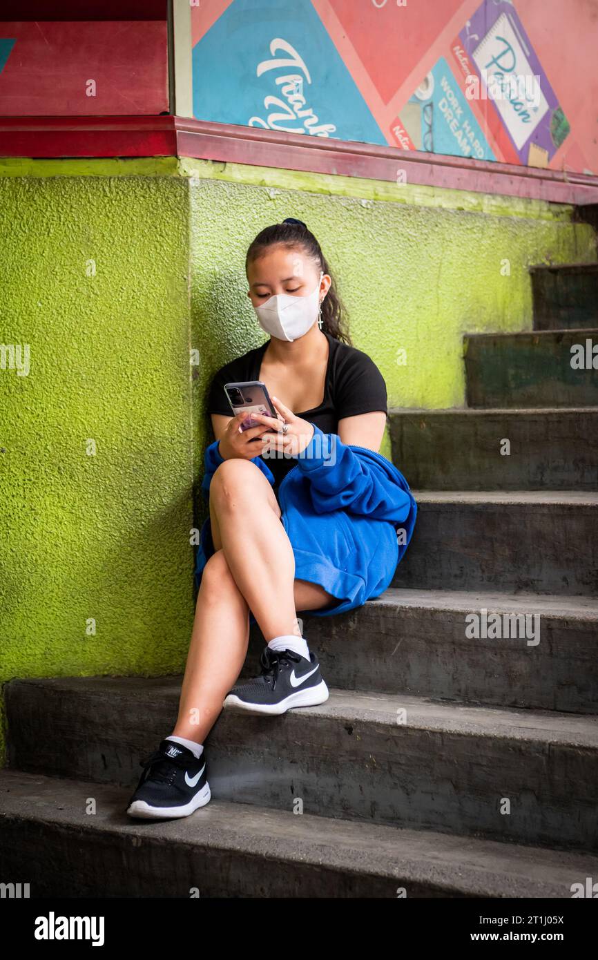 A young Filipino woman checks her mobile phone sat on some steps ...