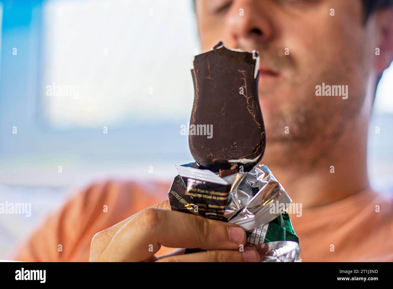 man eats chocolate ice cream with coconut filling, biting pieces onto ...
