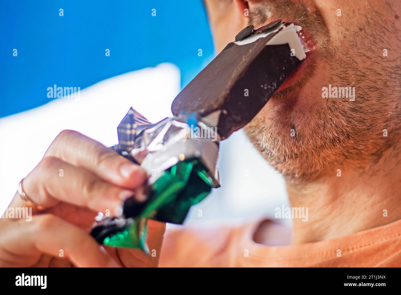 man eats chocolate ice cream with coconut filling, biting pieces onto ...