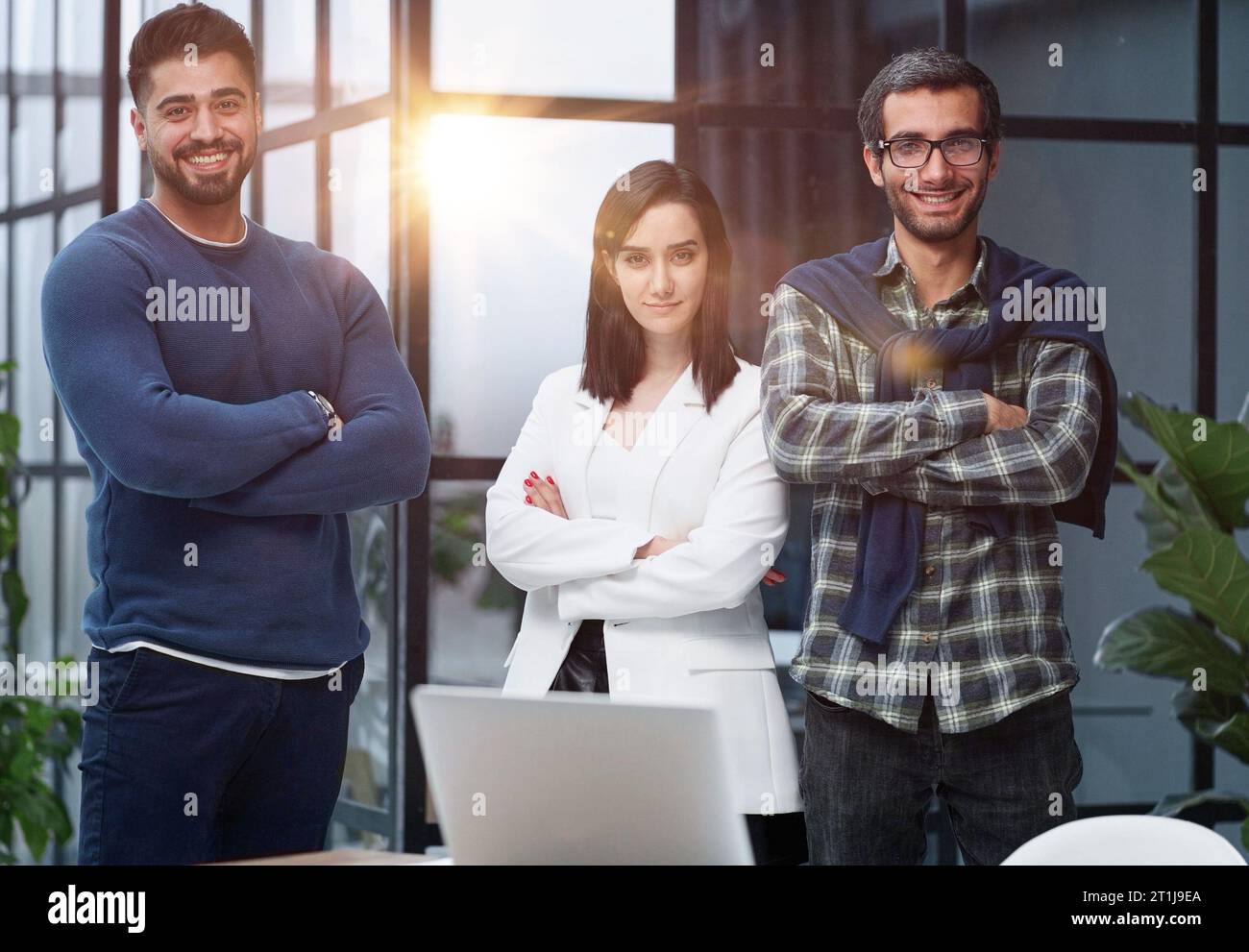 three colleagues stand in the lobby of a modern office with their arms ...
