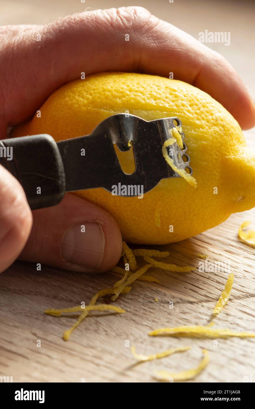 Man zesting a lemon with a lemon zester on a wooden chopping board ...