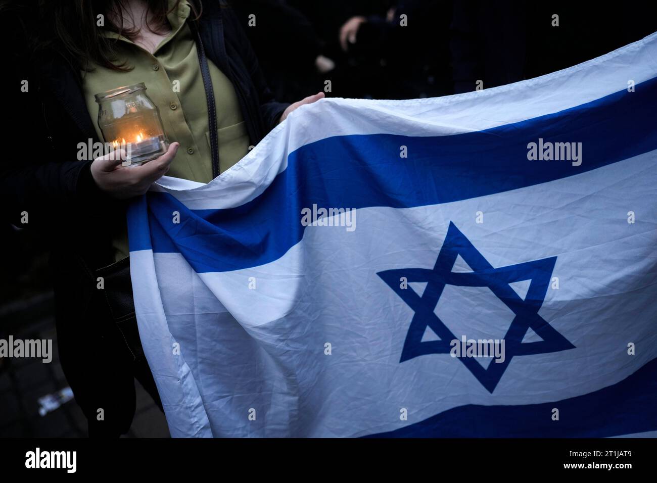 A woman holds a candle and an Israeli flag as she attends a vigil in ...