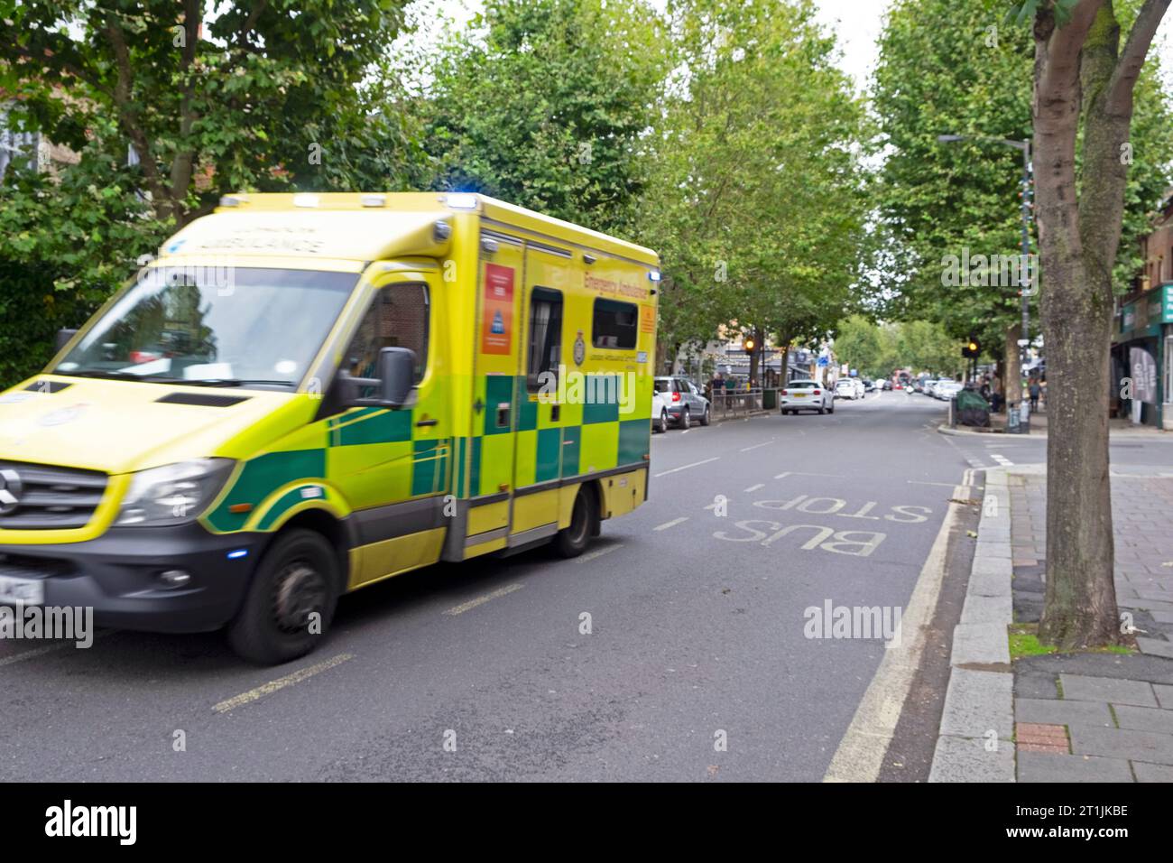 NHS ambulance side on in motion driving along tree lined street ...