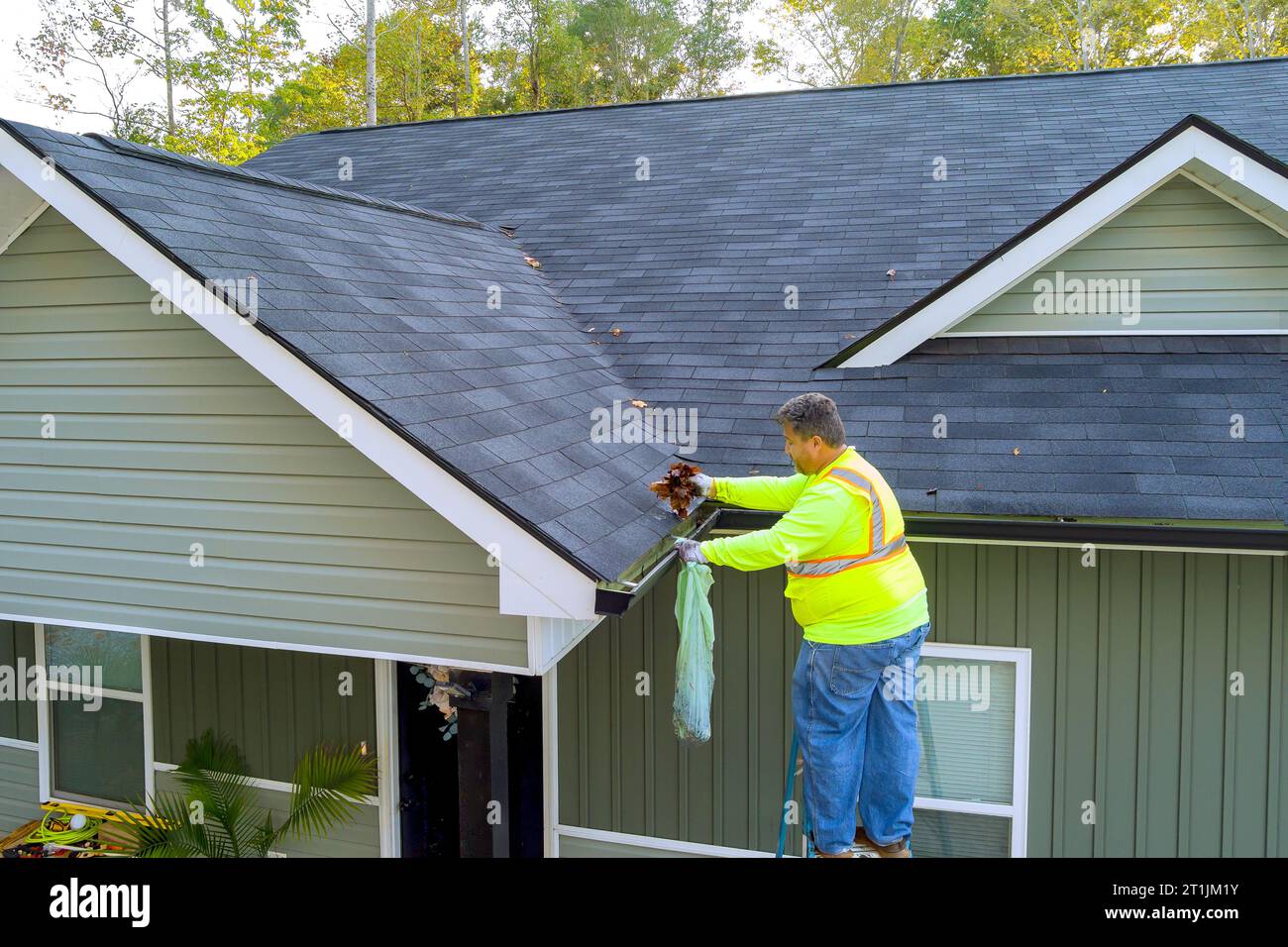 Worker is cleaning clogged roof gutter from dirt, debris fallen leaves ...