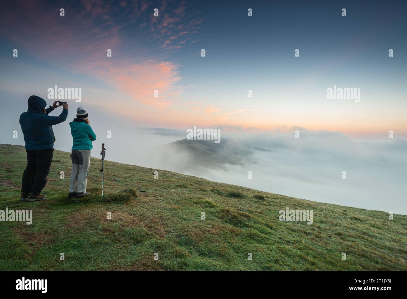 A couple watch a cloud inversion at sunrise on Mam Tor in Derbyshire ...