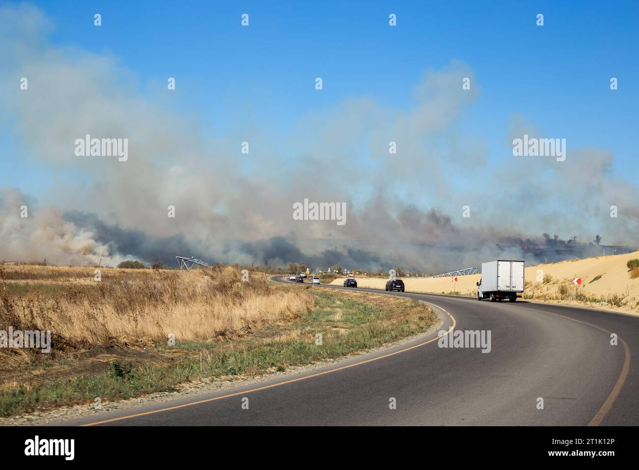 A large fire on the side of the road with vehicles moving. Smoke and ...