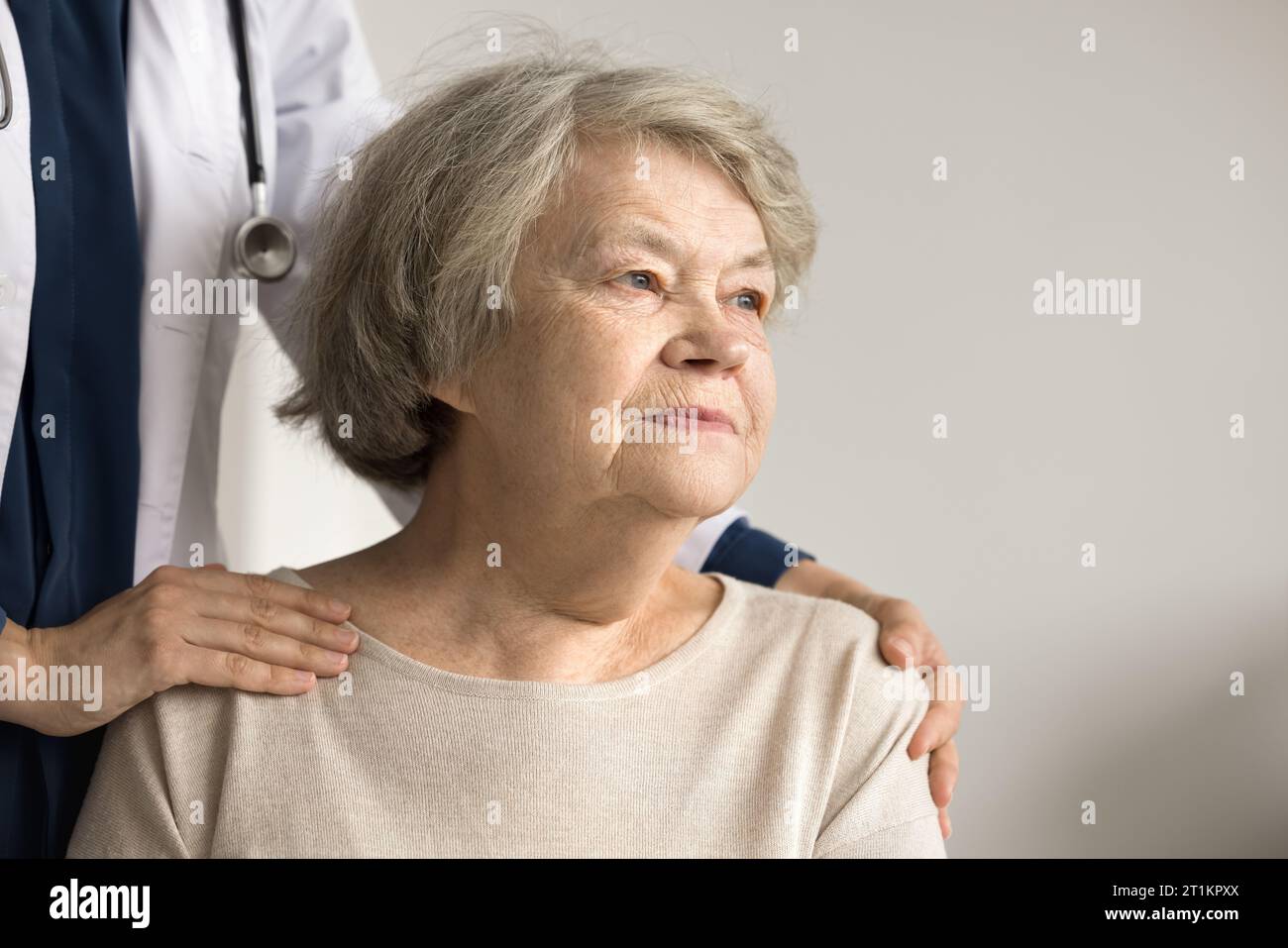 Older woman looking into distance, therapist touch shoulders supporting ...