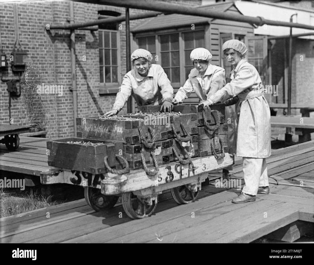 Three munitions workers, wearing white caps, overalls and trousers ...
