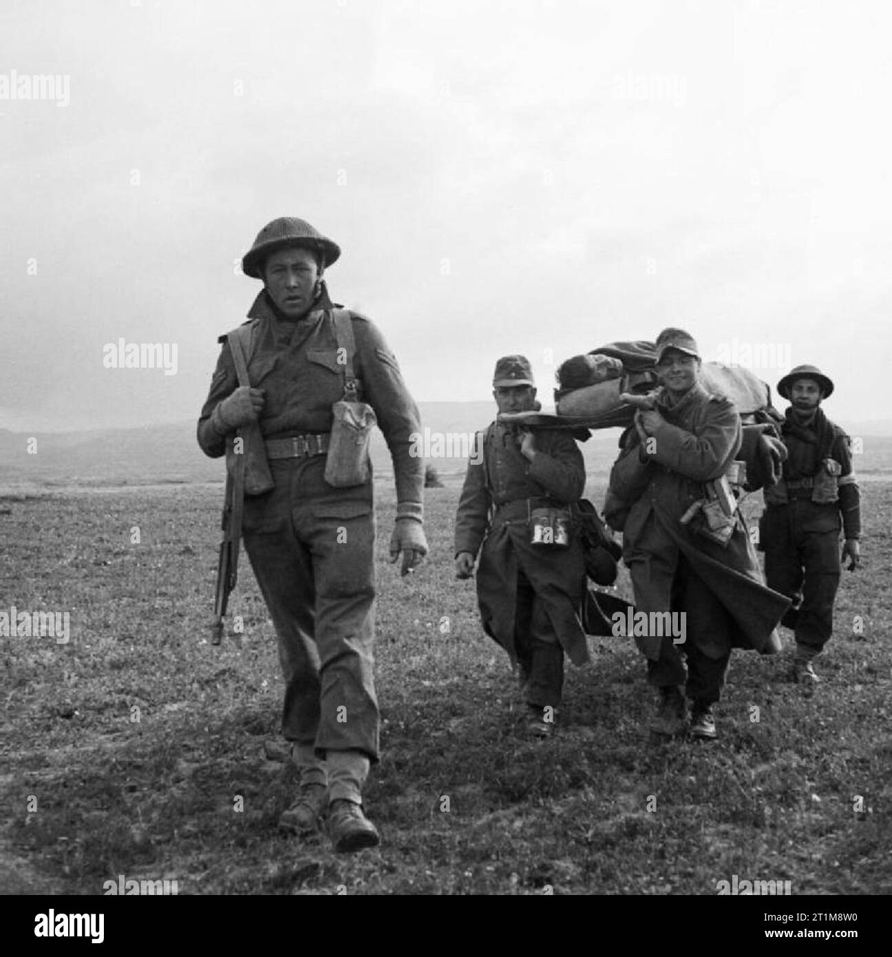German POWs help carry a wounded British soldier during 6th Armoured ...