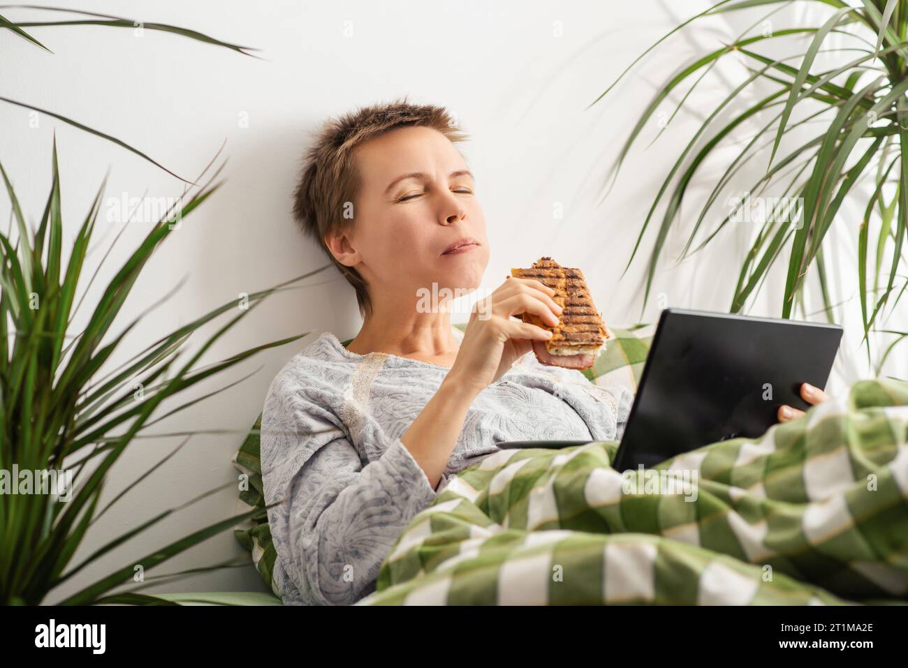 Throughout the day, a middle-aged woman with short hair lounges in bed ...