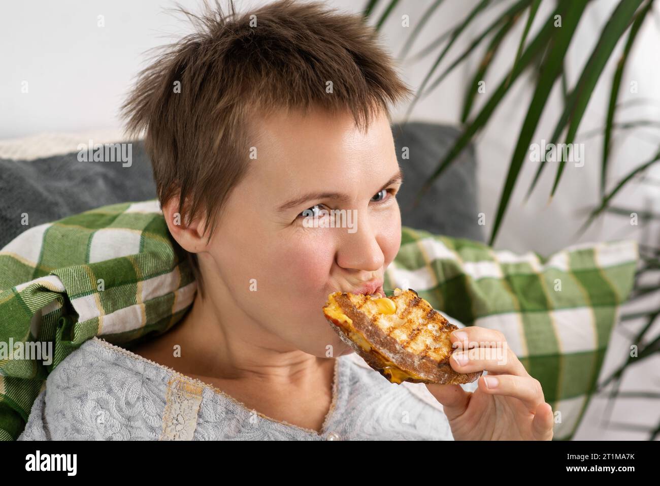 A woman eats a sandwich in bed. A middle-aged woman with short hair ...