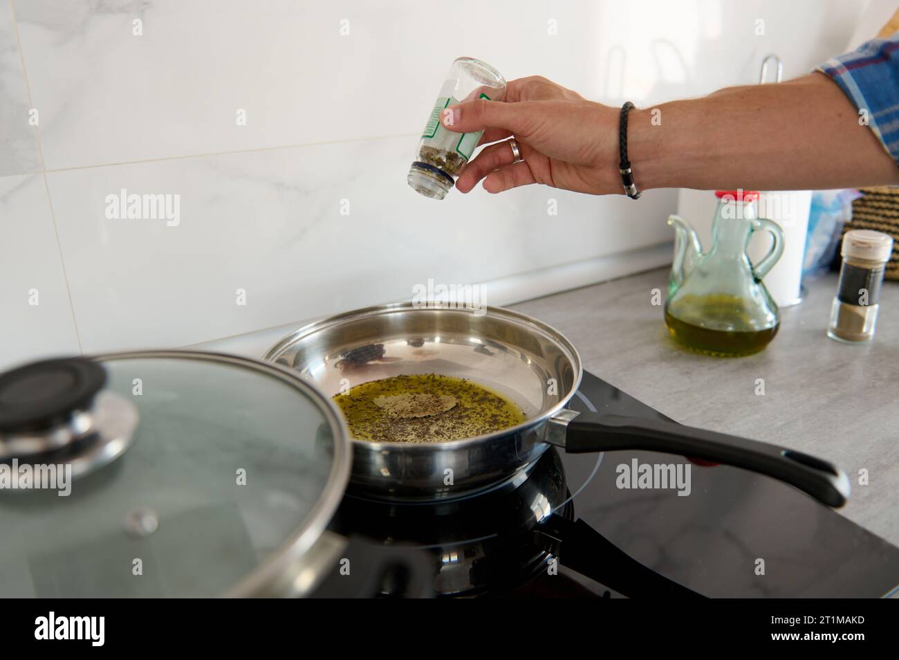 Close-up of chef hand adding pepper into a frying pan with bay leaf and ...