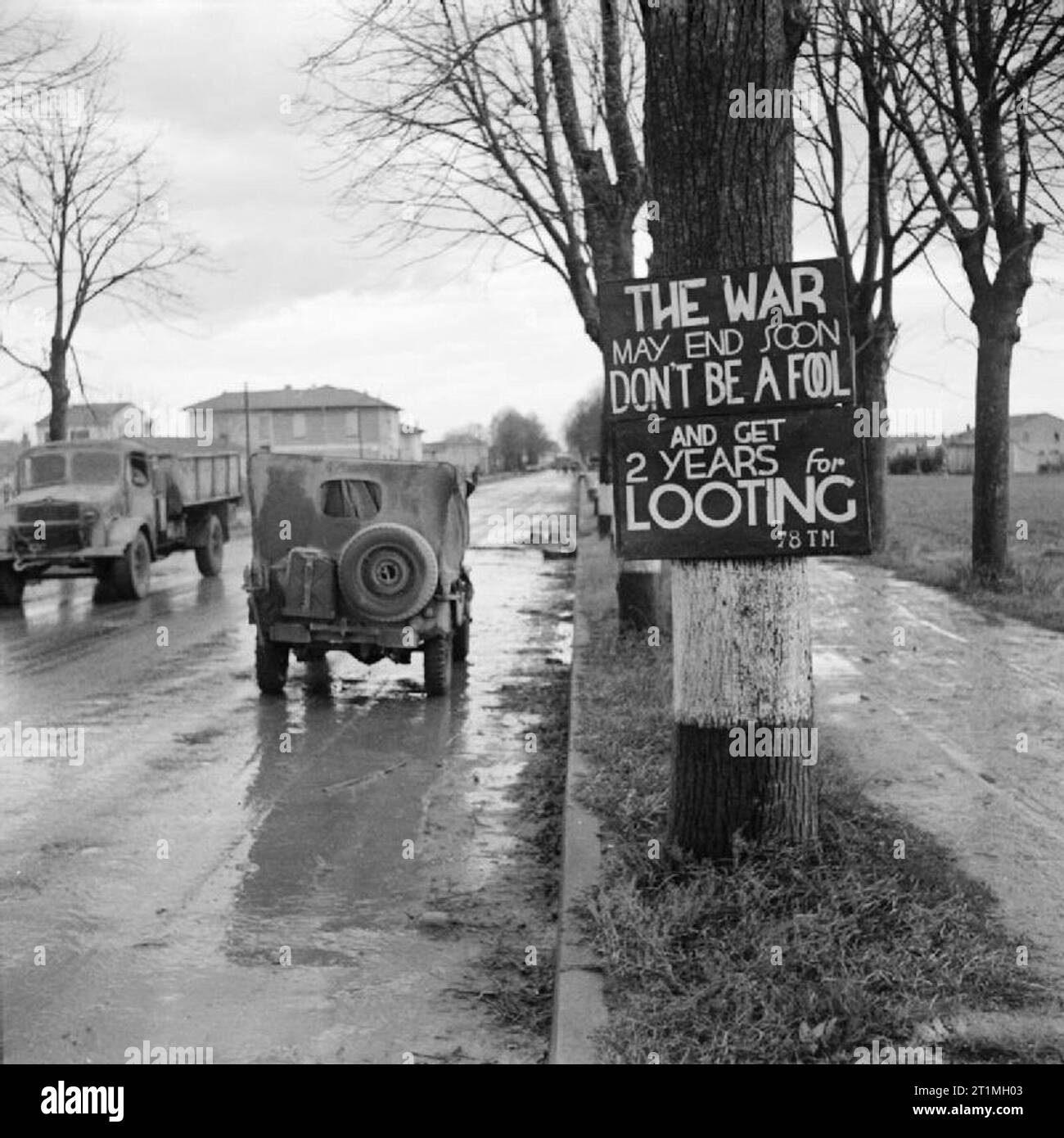 A British jeep passes a sign warning against looting on the outskirts ...