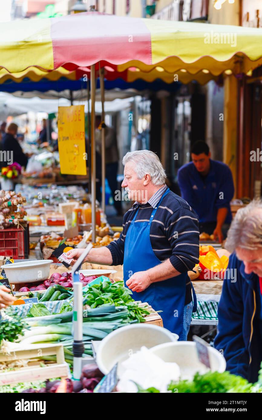 A local French male stallholder at a vegetable stall hands change to a ...