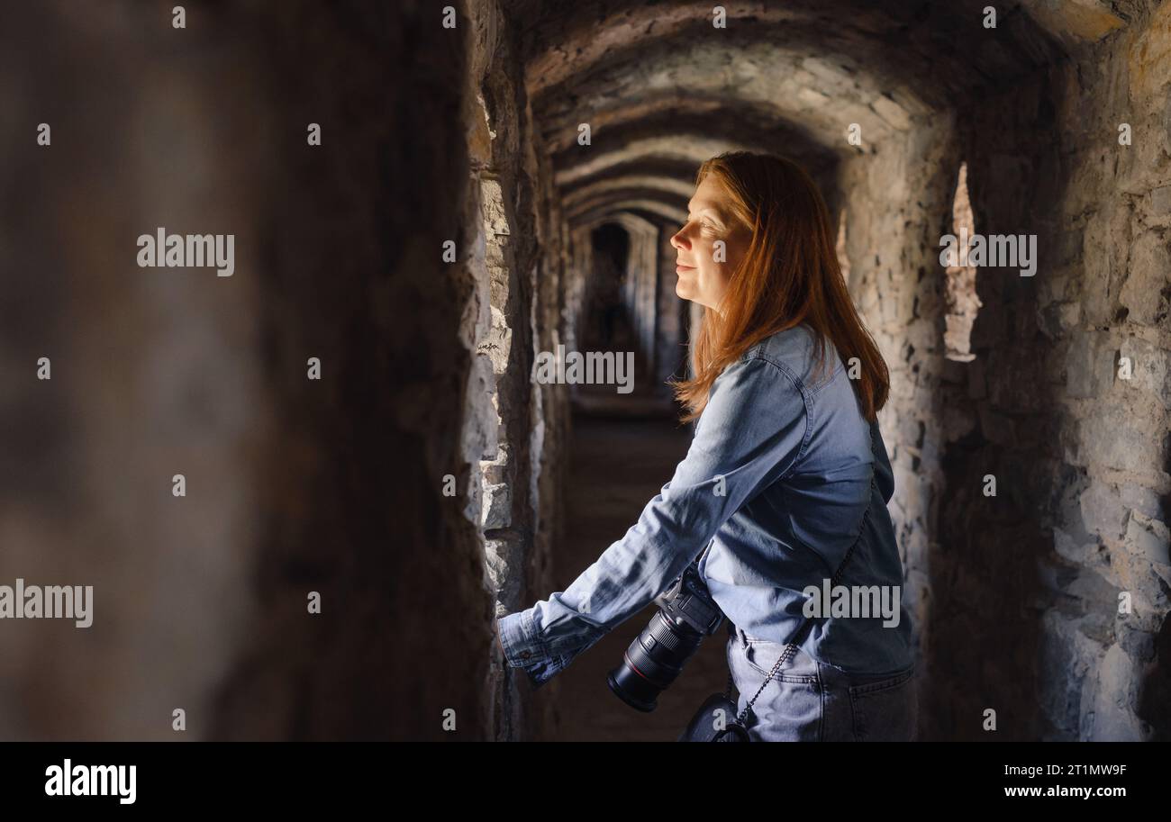 Woman walking through old tunnel, looking in window and taking pictures ...