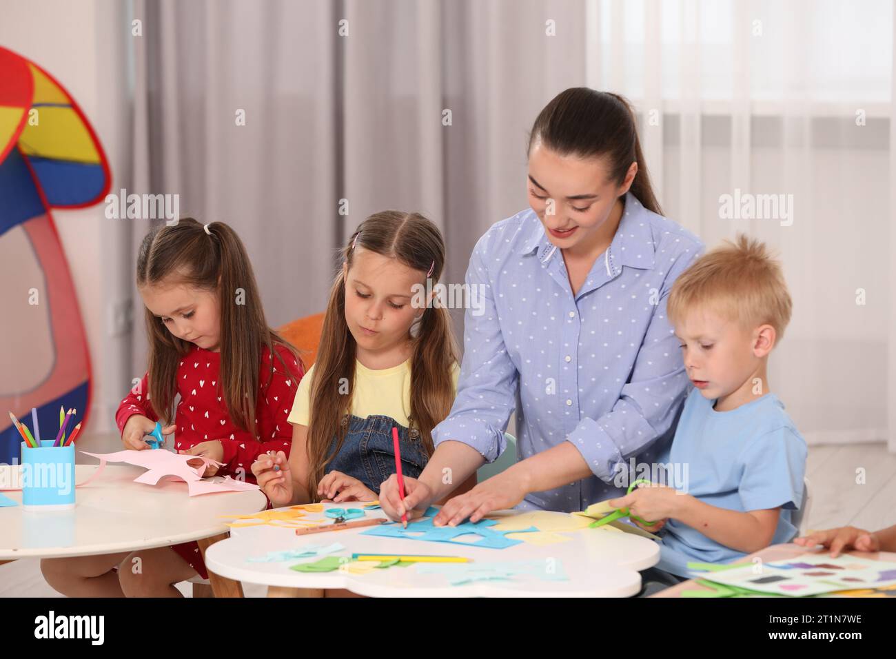 Nursery teacher and group of cute little children making toys from ...