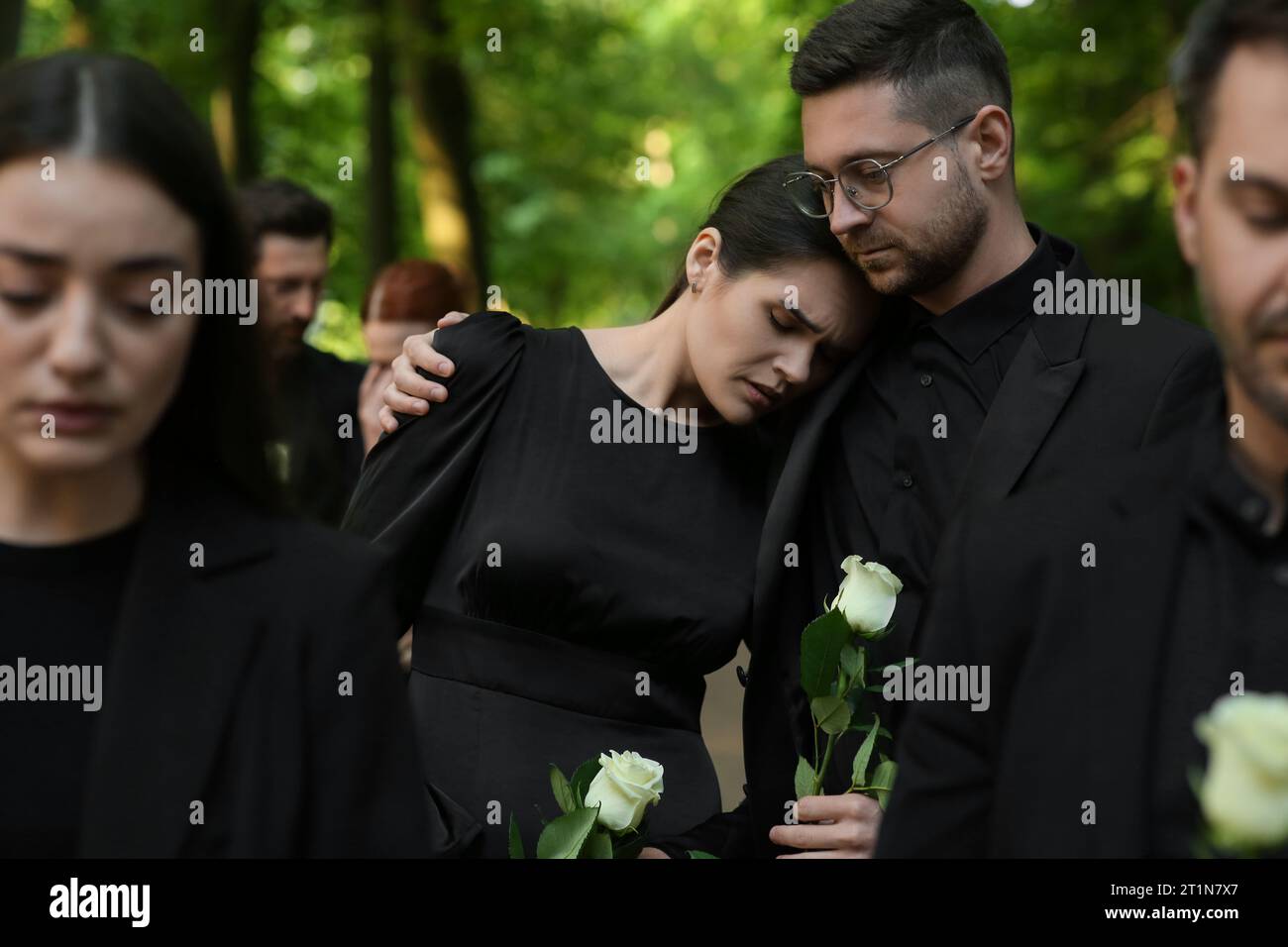 Funeral ceremony. Sad people with white rose flowers mourning outdoors ...